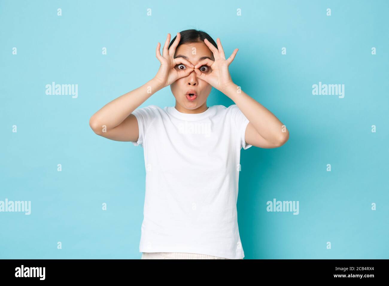 Surprised and amazed funny asian girl in white t-shirt looking through ...