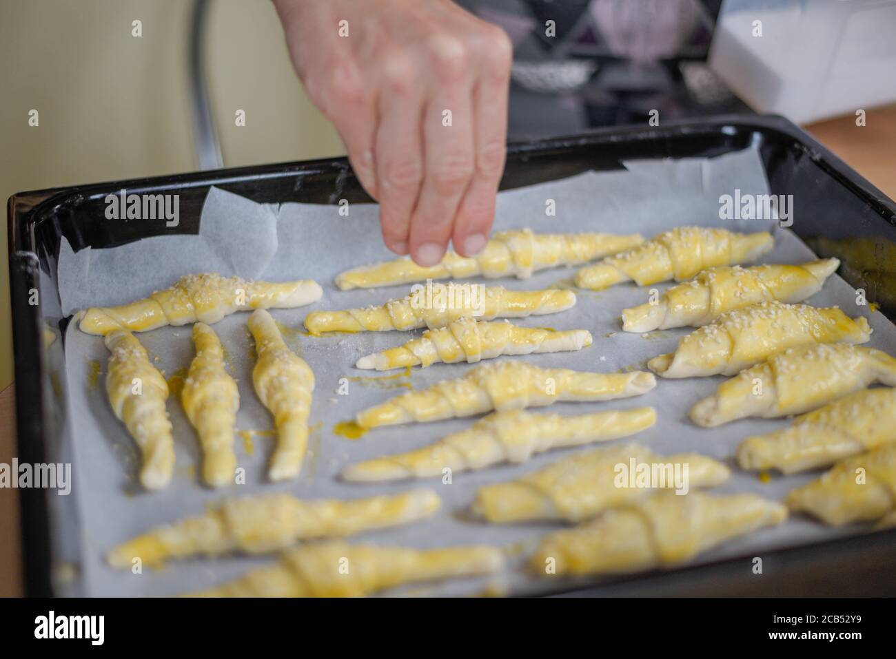 Closeup shot of a person pouring seed toppings onto rolled up pastries ...