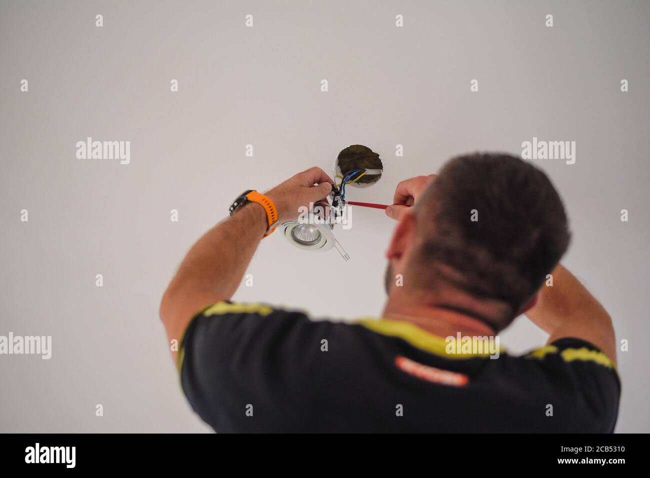 Back view of a handyman fixing electricity wires in a white wall Stock ...