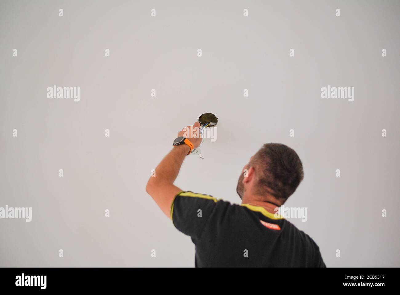Back view of a handyman fixing electricity wires in a white wall Stock ...