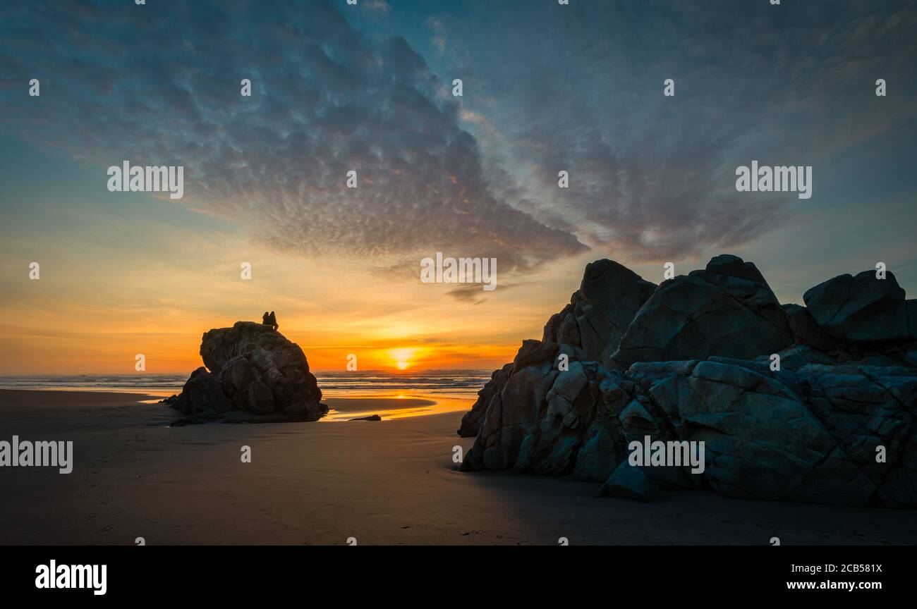 People sit on rock watching dramatic sunset at Oregon coast Stock Photo ...