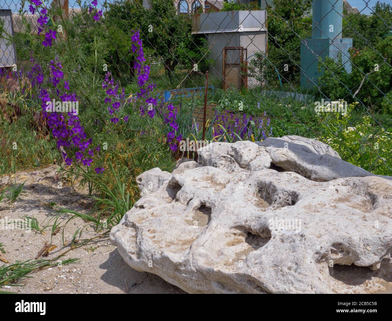 Huge porous rock with big holes on a sand in front of a mesh fence and ...