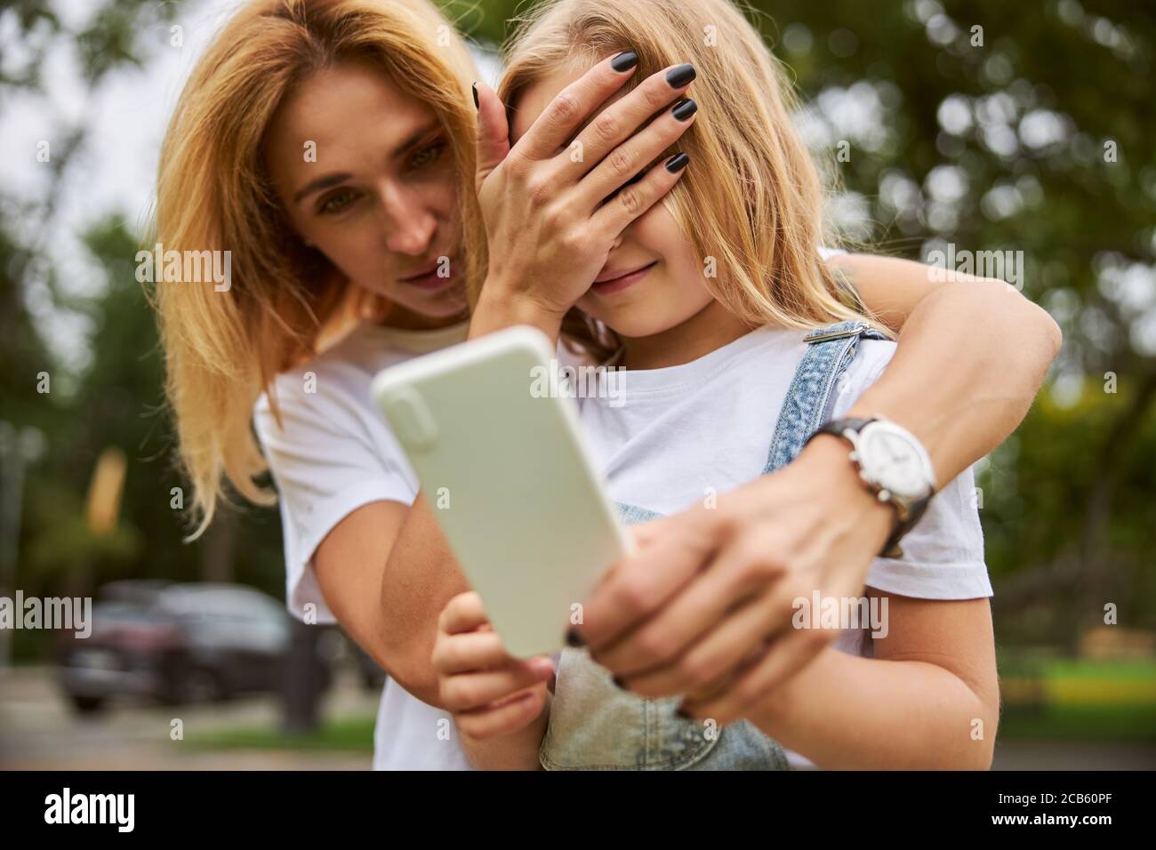 Beautiful blonde female turning a blind eyes with hand to her daughter ...