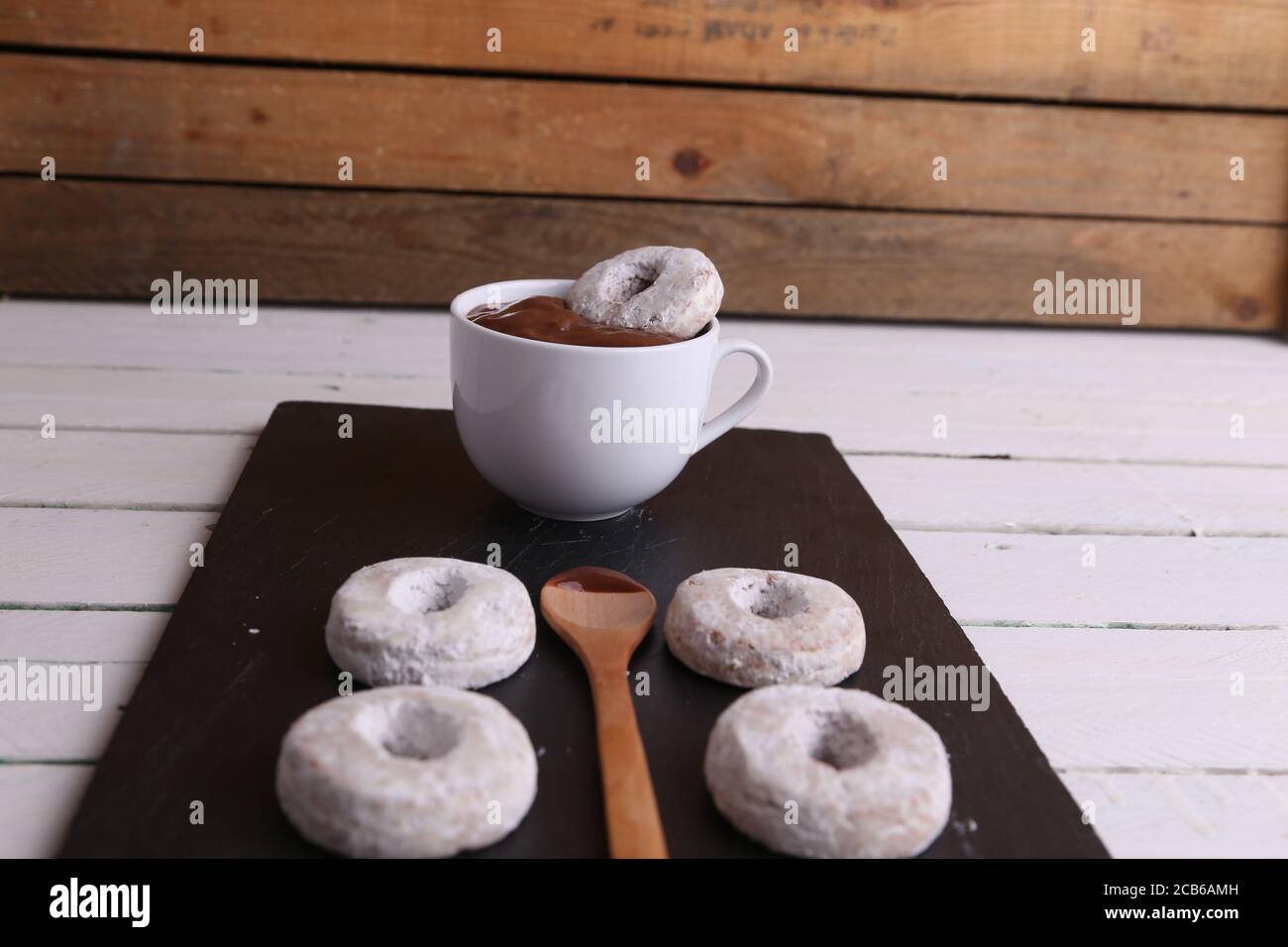 Cup of hot chocolate, doughnuts and a spoon on a black wooden board ...