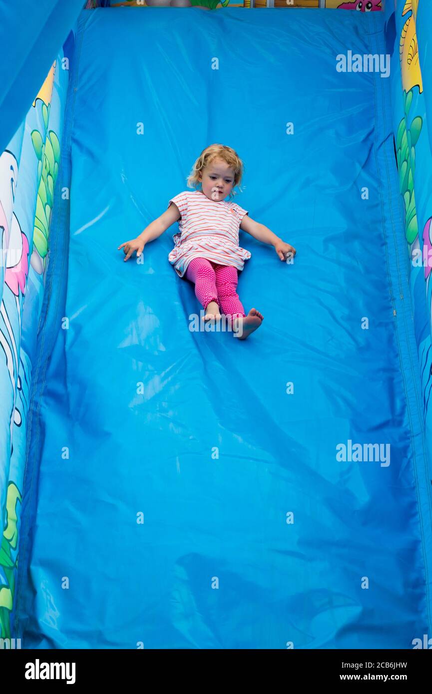 Cute blonde girl riding an inflatable slide Stock Photo - Alamy