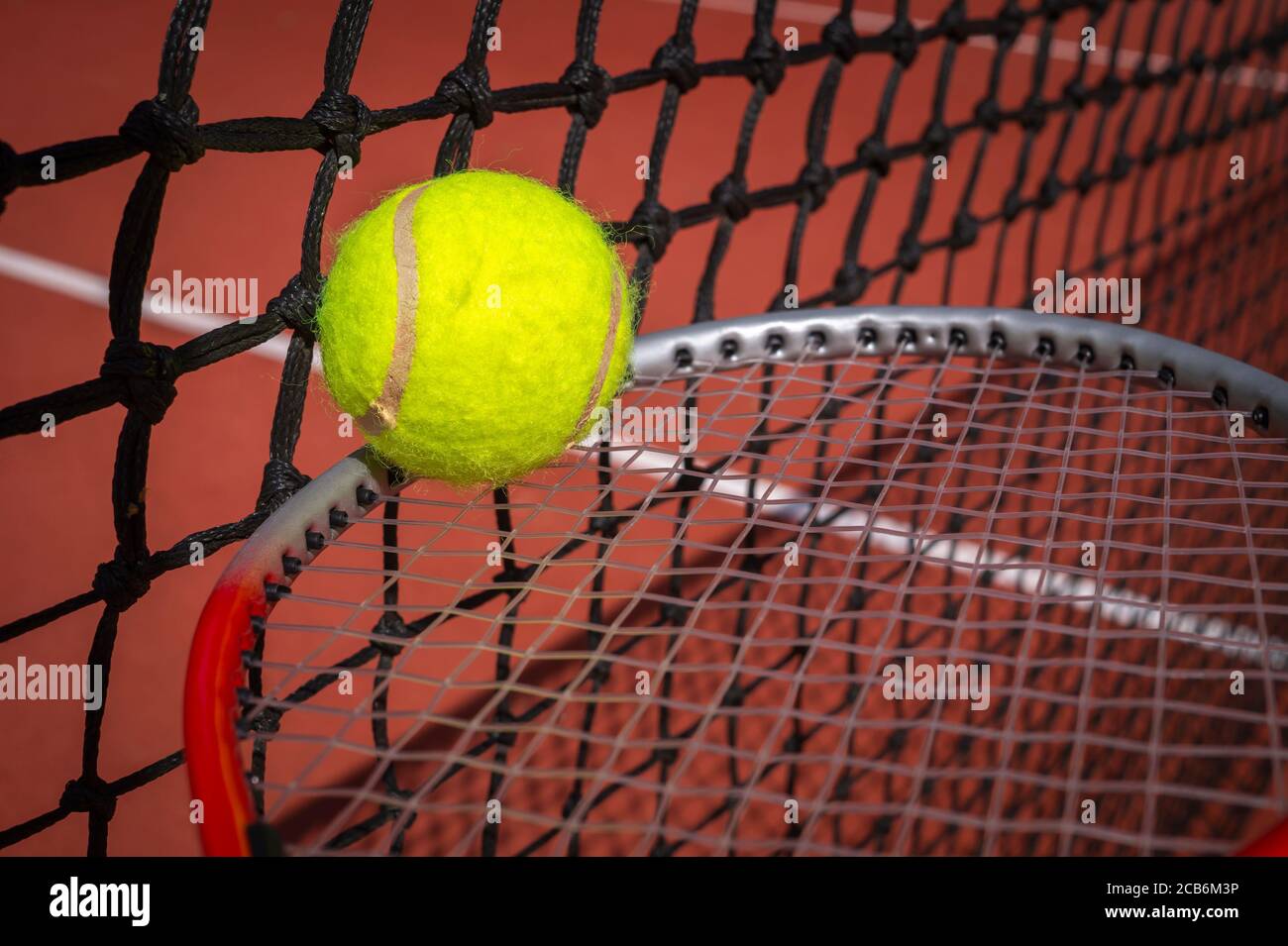 Tennis balancing ball on a racket alongside a net on a court in a sport ...