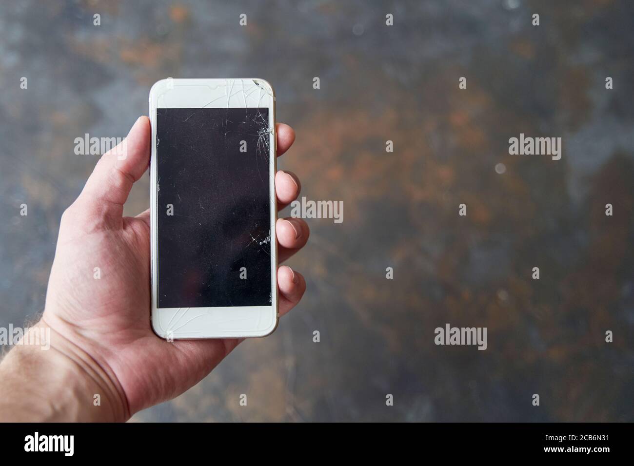A young man holds a smartphone with a broken screen in his hand on a ...
