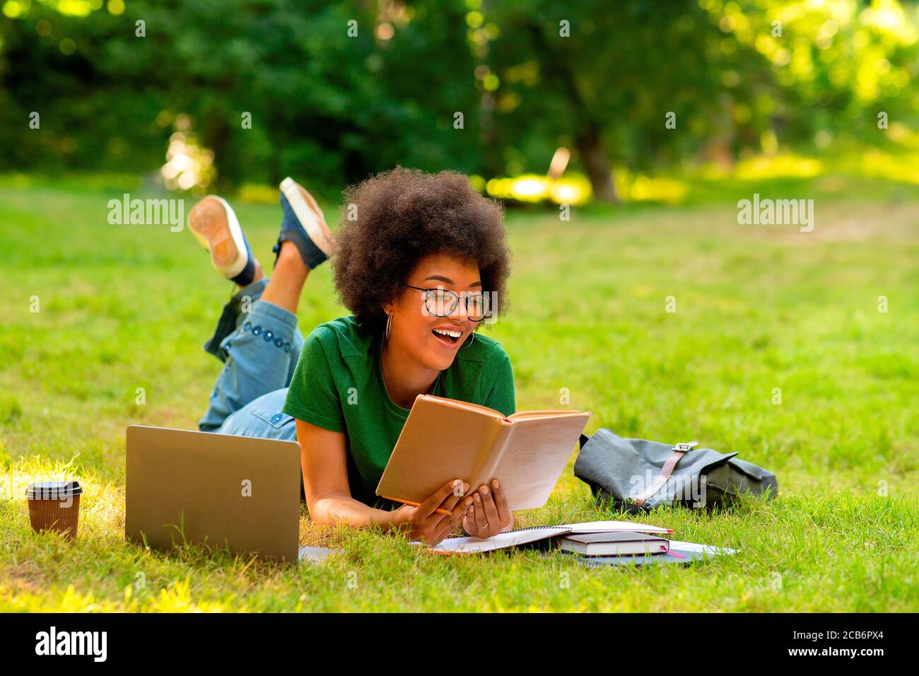 Cheerful African Student Girl Reading Books Outdoors, Lying On Lawn In ...