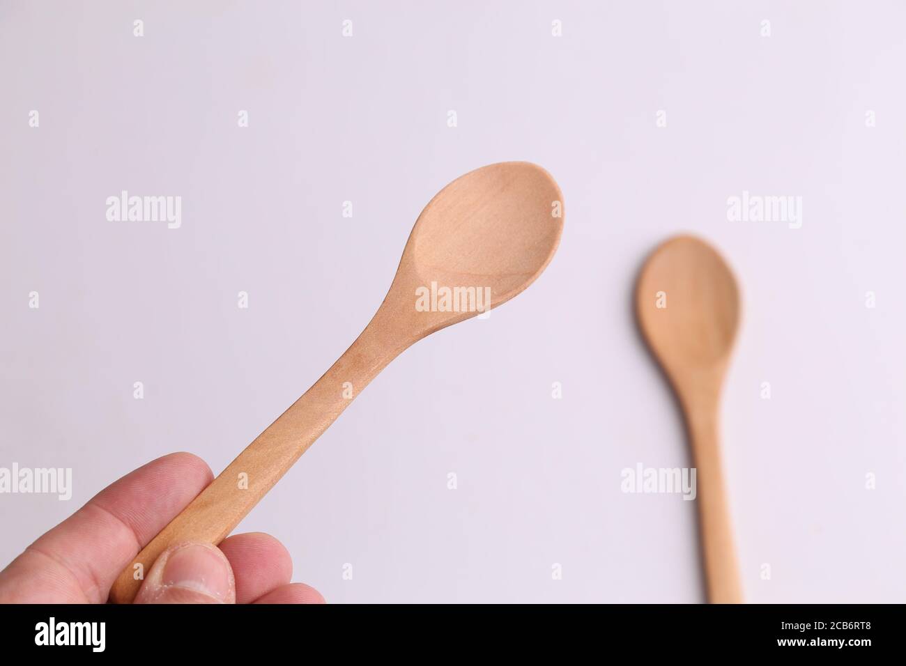 High angle shot of a person holding a wooden spoon over a white surface ...