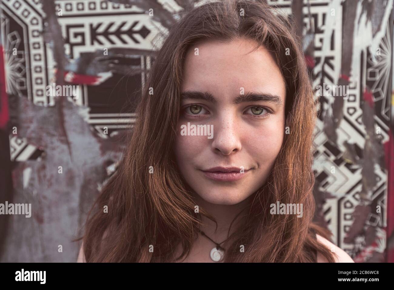 Portrait of a young smiling woman in front of a wall with torn posters ...