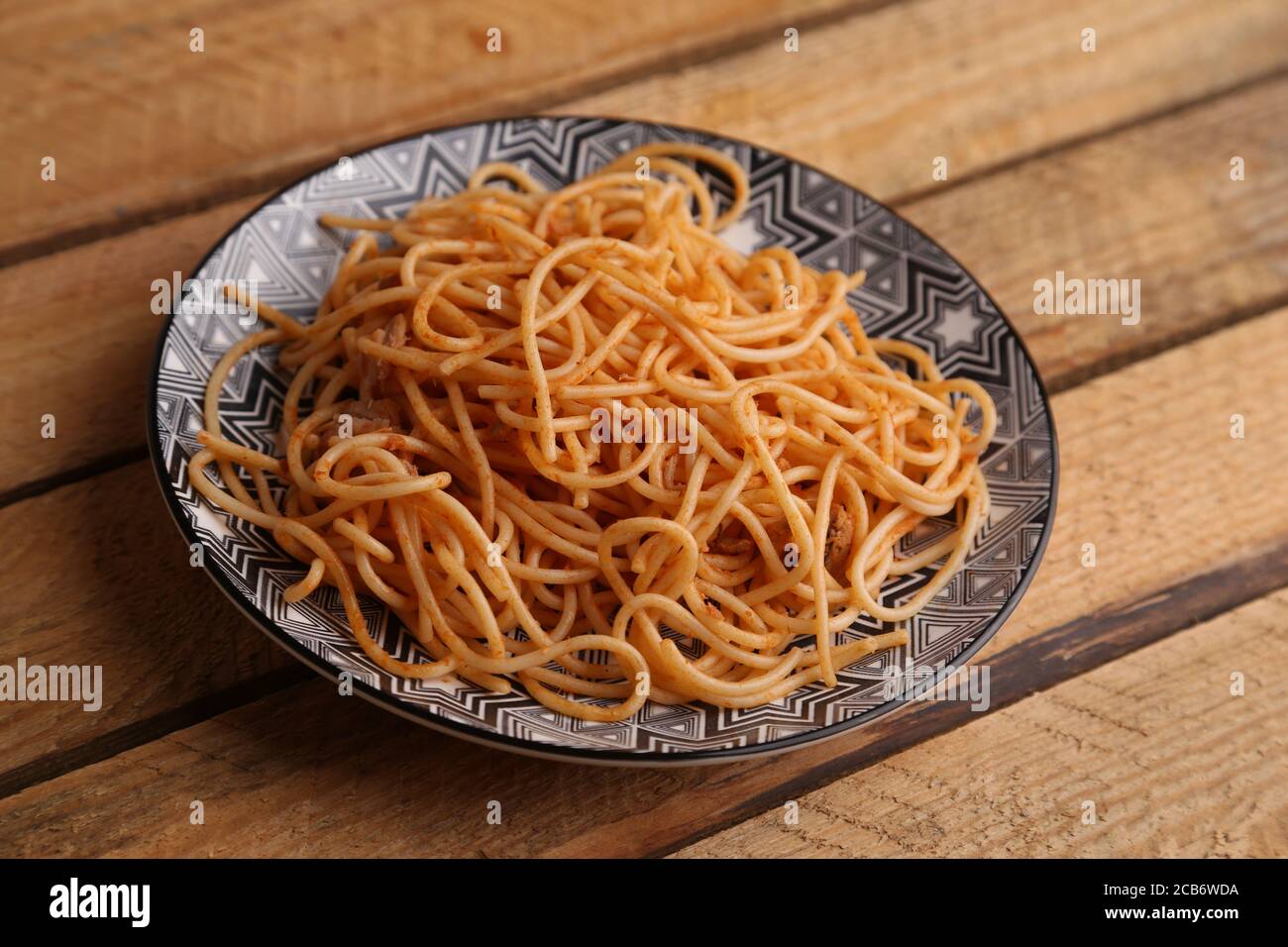 High angle shot of spaghetti noodles on a patterned plate on a wooden ...