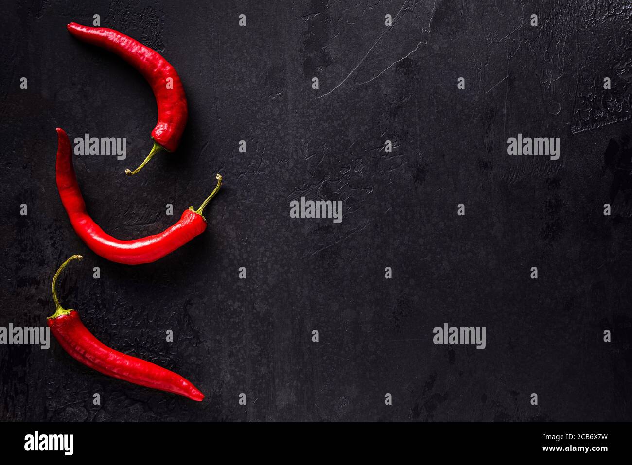 Three curved whole bright red chilli peppers on textured black stone ...