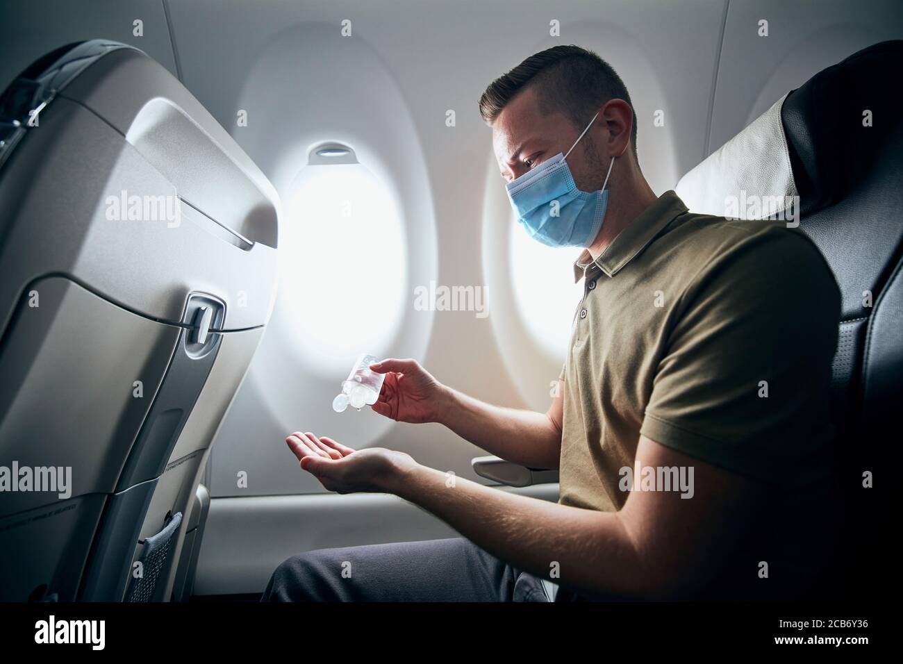Man wearing face mask and using hand sanitizer inside airplane during ...
