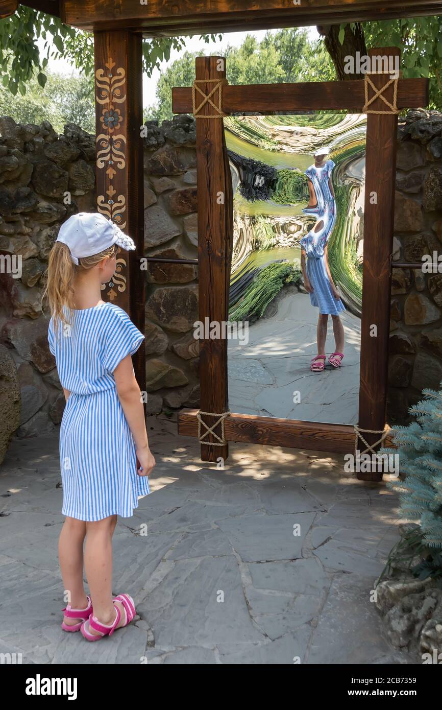little girl in front of distorting mirror. funhouse mirror in a park ...