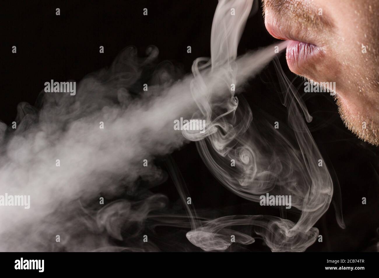 man mouth exhales a stream of cigarette smoke on a dark background ...