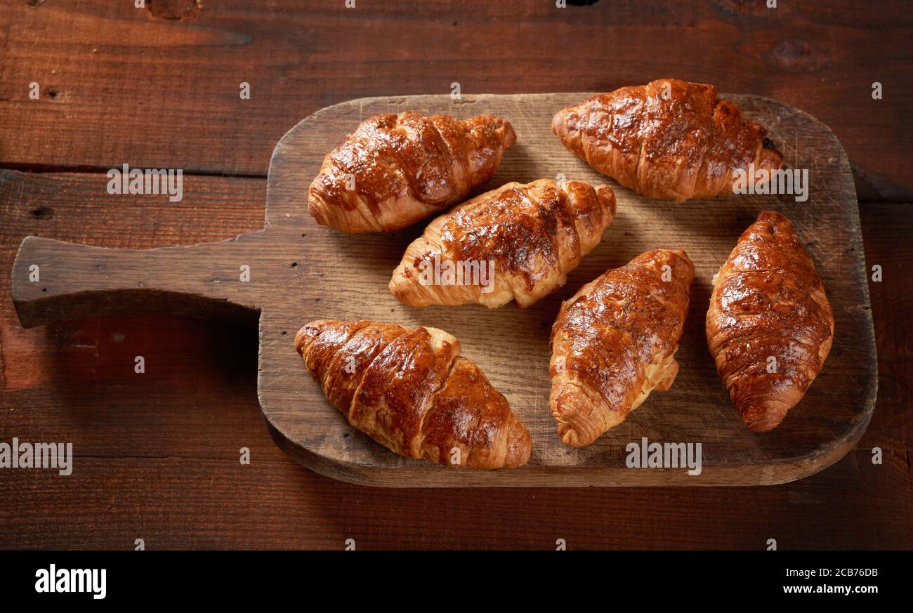 baked croissants on a wooden brown board, delicious and appetizing ...