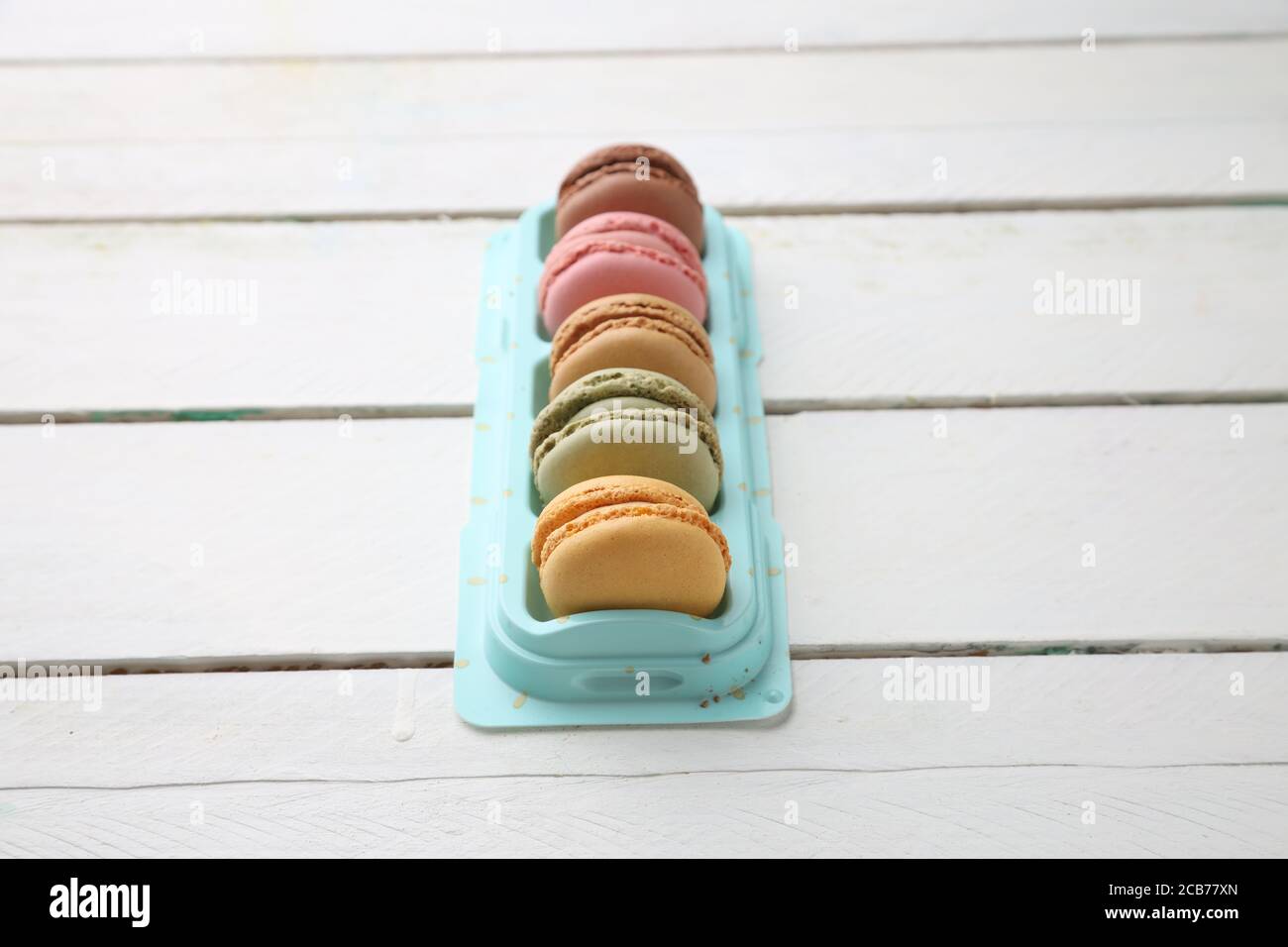 Row of colorful macarons in a blue carton on a white kitchen table ...
