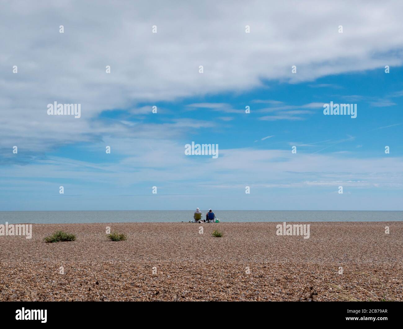 Two people sitting on the shingle beach alone in wide open space at ...