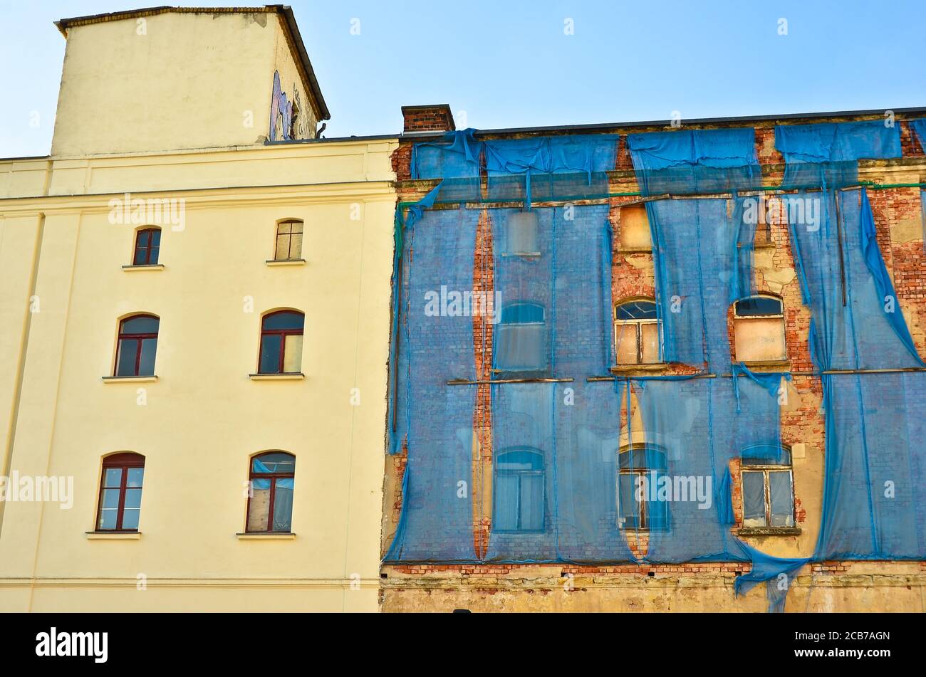 The facade of an old ruinous building is mantled with some blue ...