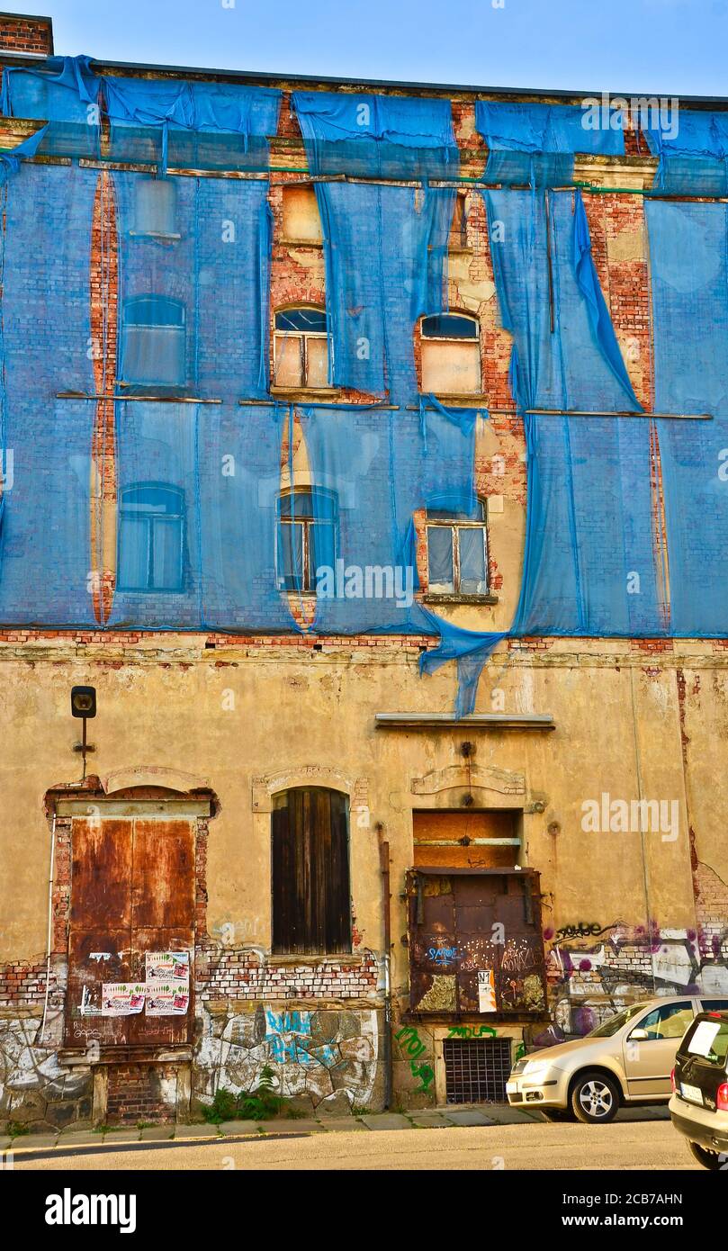 The facade of an old ruinous building is mantled with some blue ...