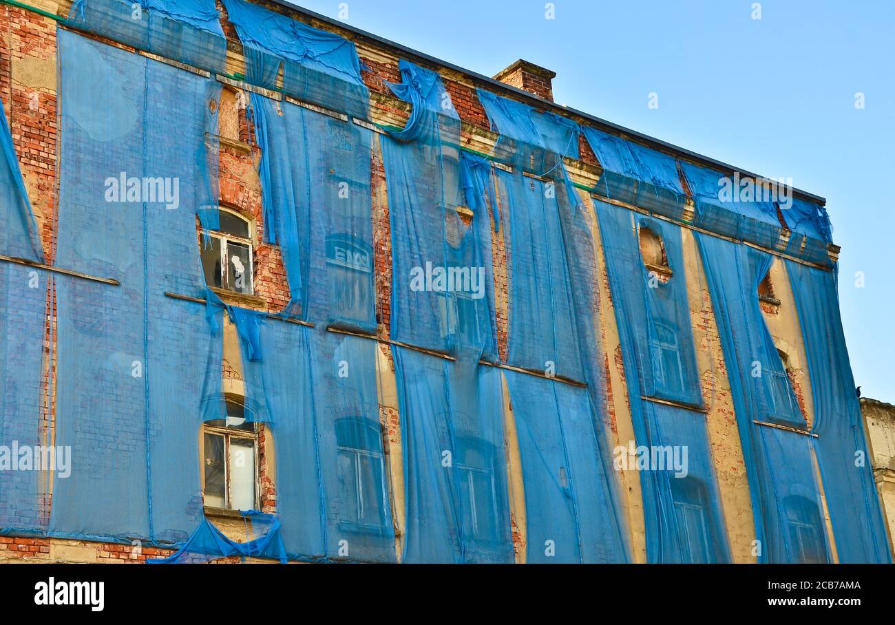 The facade of an old ruinous building is mantled with some blue ...