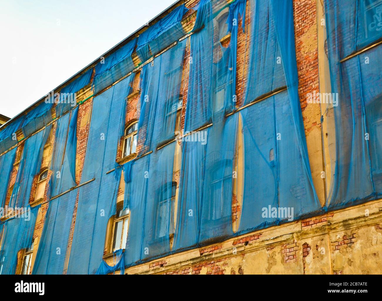 The facade of an old ruinous building is mantled with some blue ...