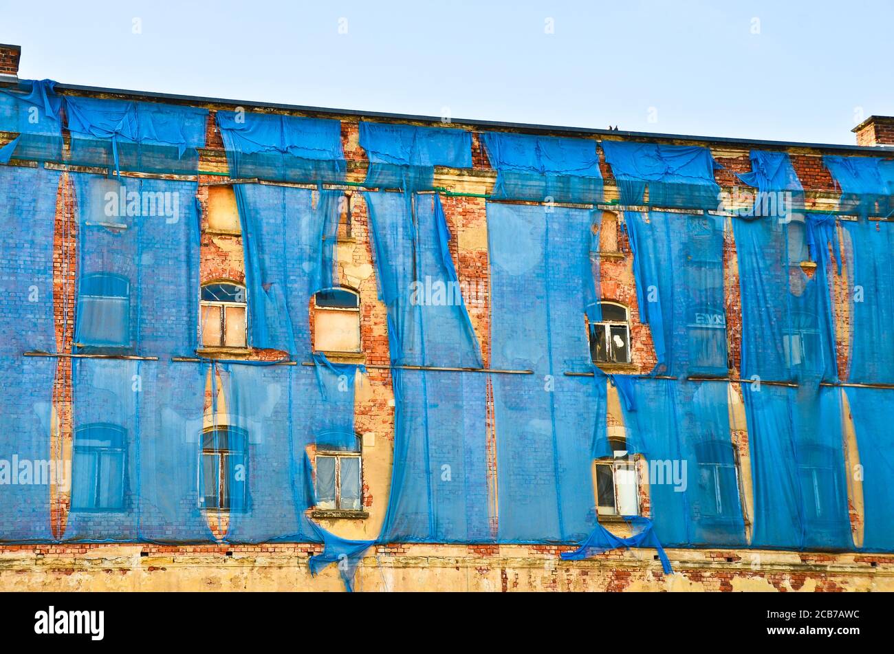 The facade of an old ruinous building is mantled with some blue ...