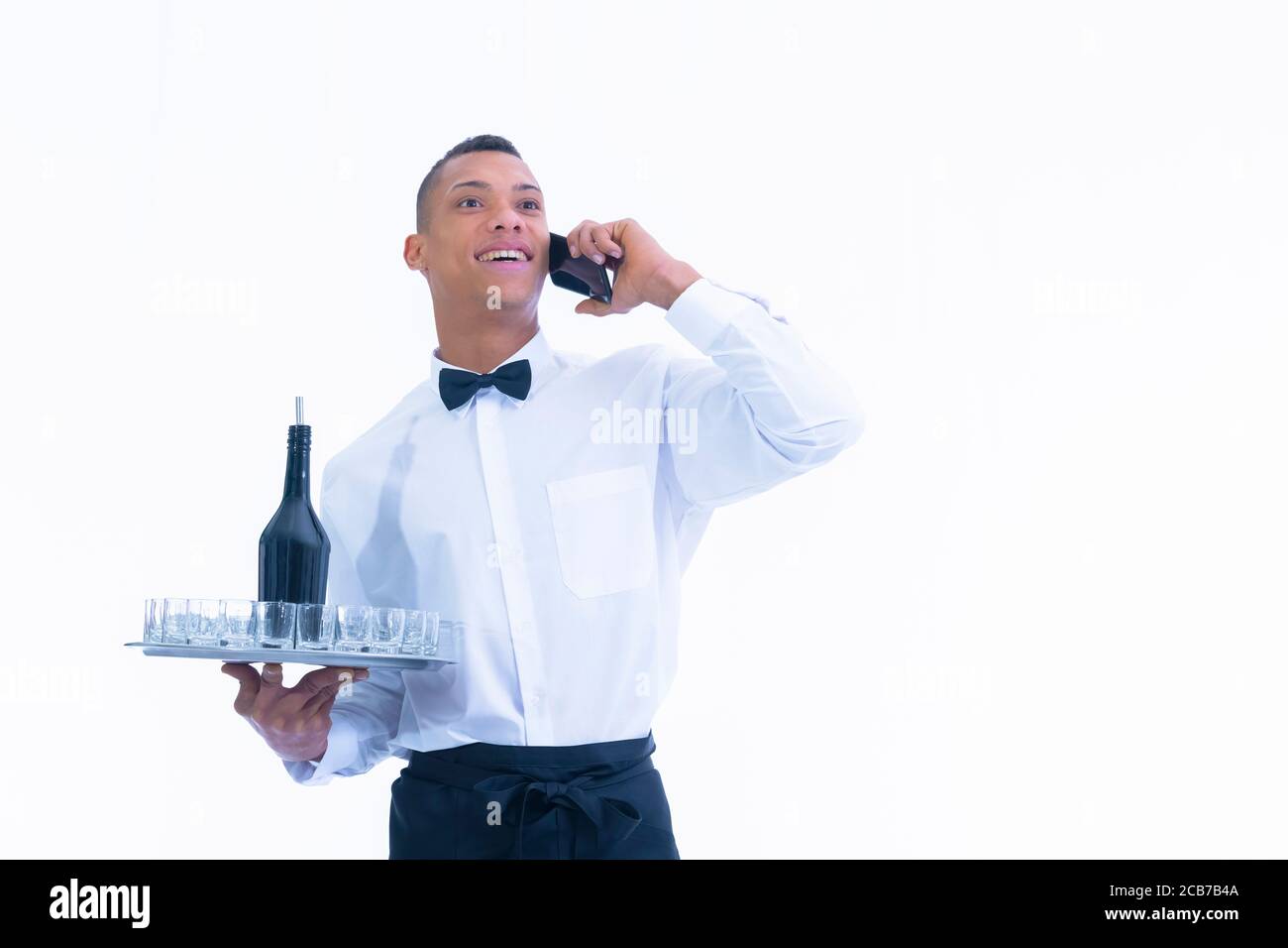 Handsome young waiter talks on his phone while holding a tray with ...