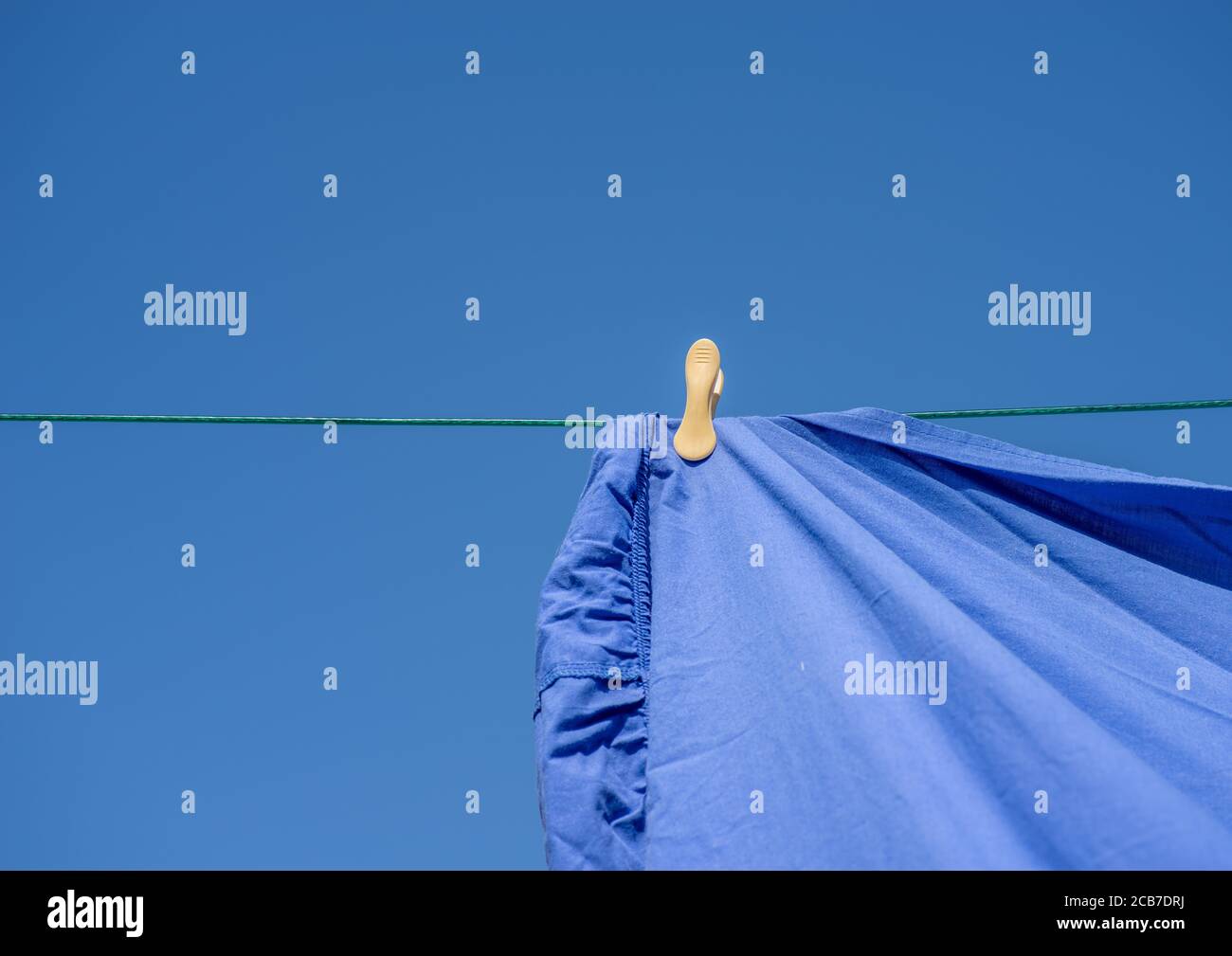 A yellow cloths peg on a washing line with a blue sheet and blue sky ...