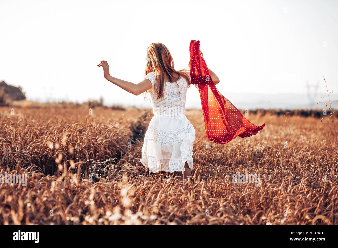Back view of young, ginger girl in white dress running through the ...