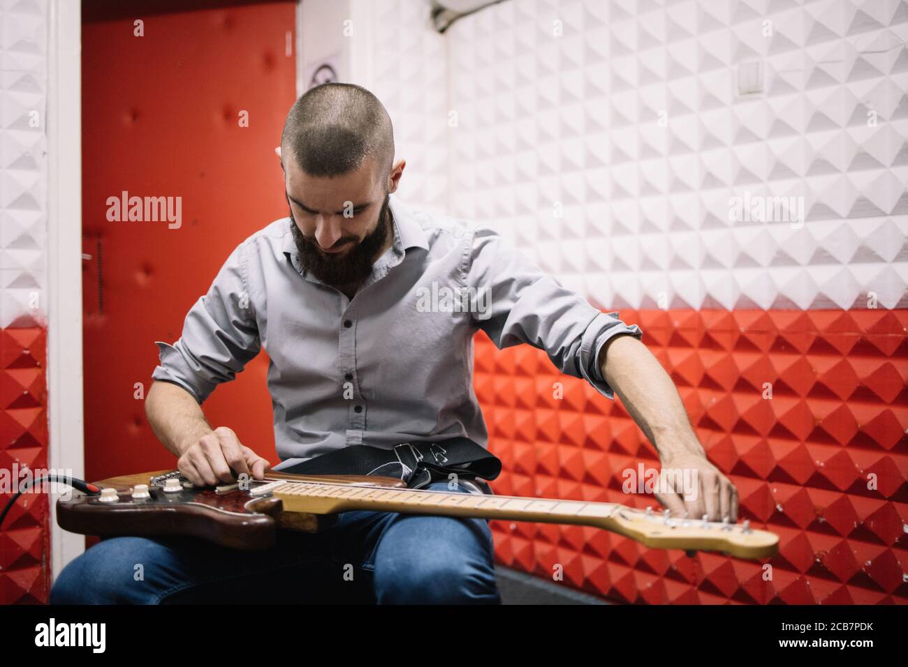 Guitar player setting tone to his music instrument in soundproof studio ...
