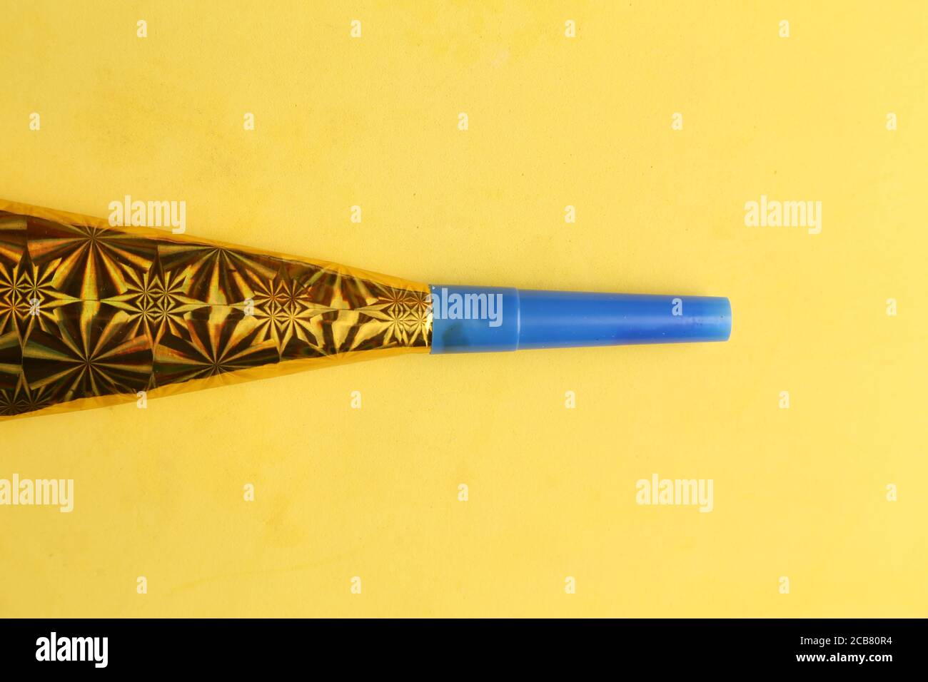 Top view of a golden cardboard party trumpet on a yellow background ...