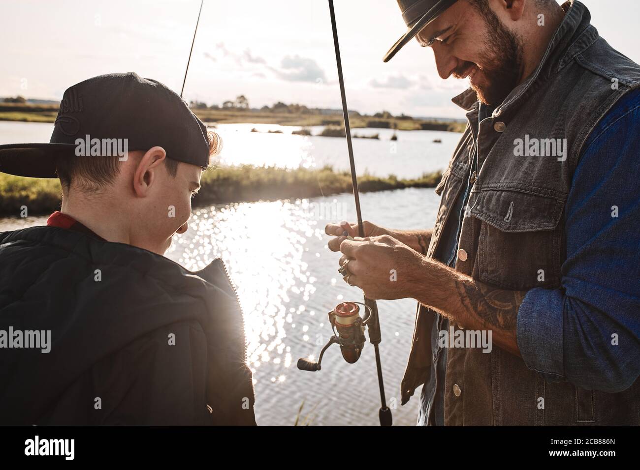 Father smile, shows and explains son how use fishing tackle. Boy watch ...