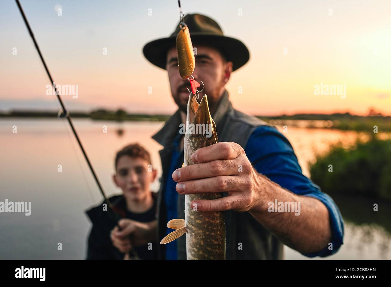 Positive man with teenager boy standing together and showing catch fish ...