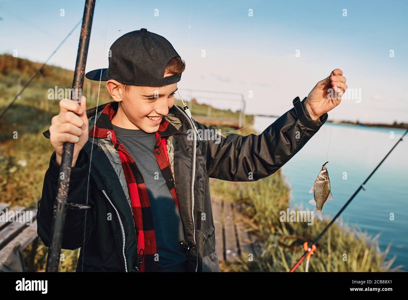 Teen caucasian boy catch first fish. He smiles, happy, look, show fish ...