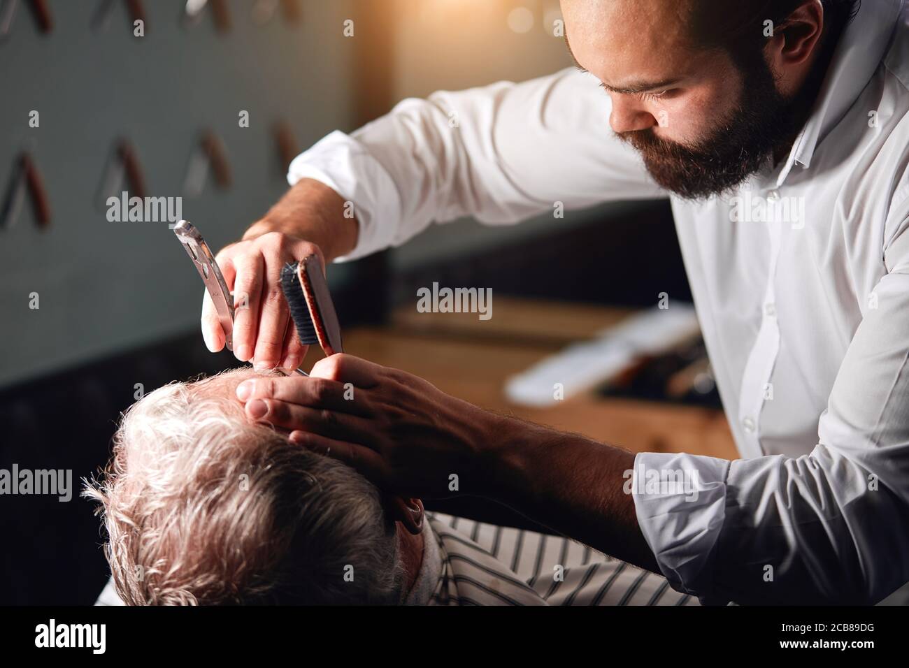 pleasant handsome stylist shaving hairs on the forehead of client ...