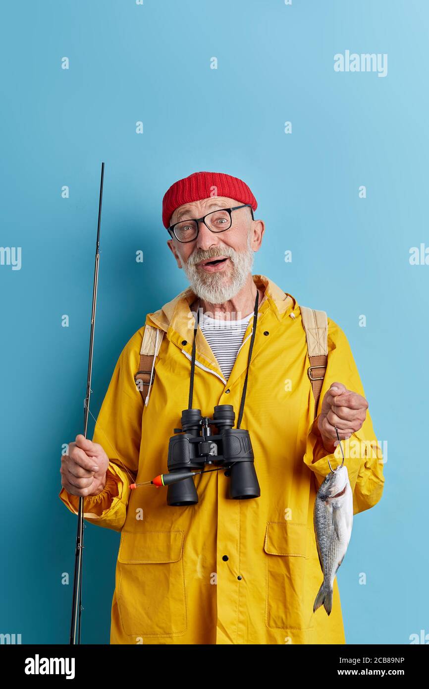 old cheerful man enjoying his fist catch, isolated blue background ...
