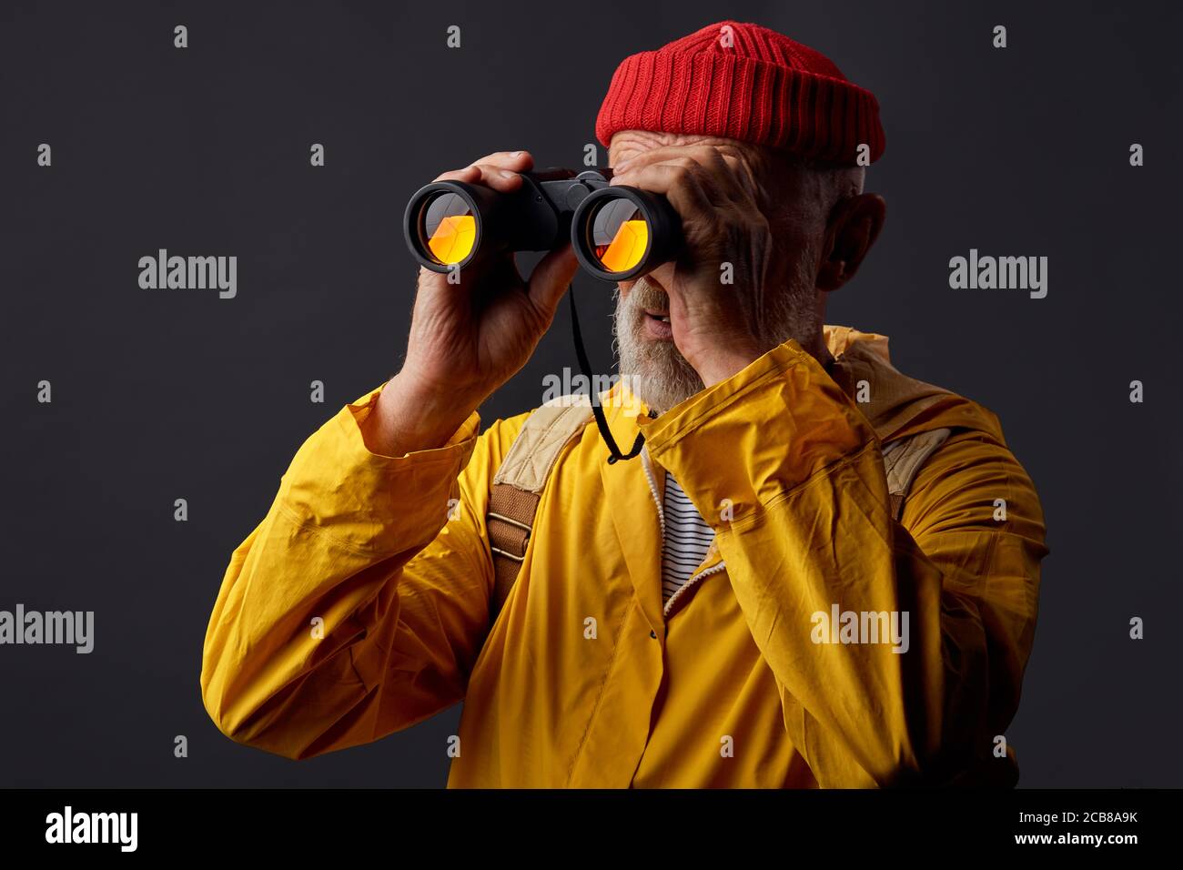 old explorer in red cap and yellow coat looking with binocular into the ...
