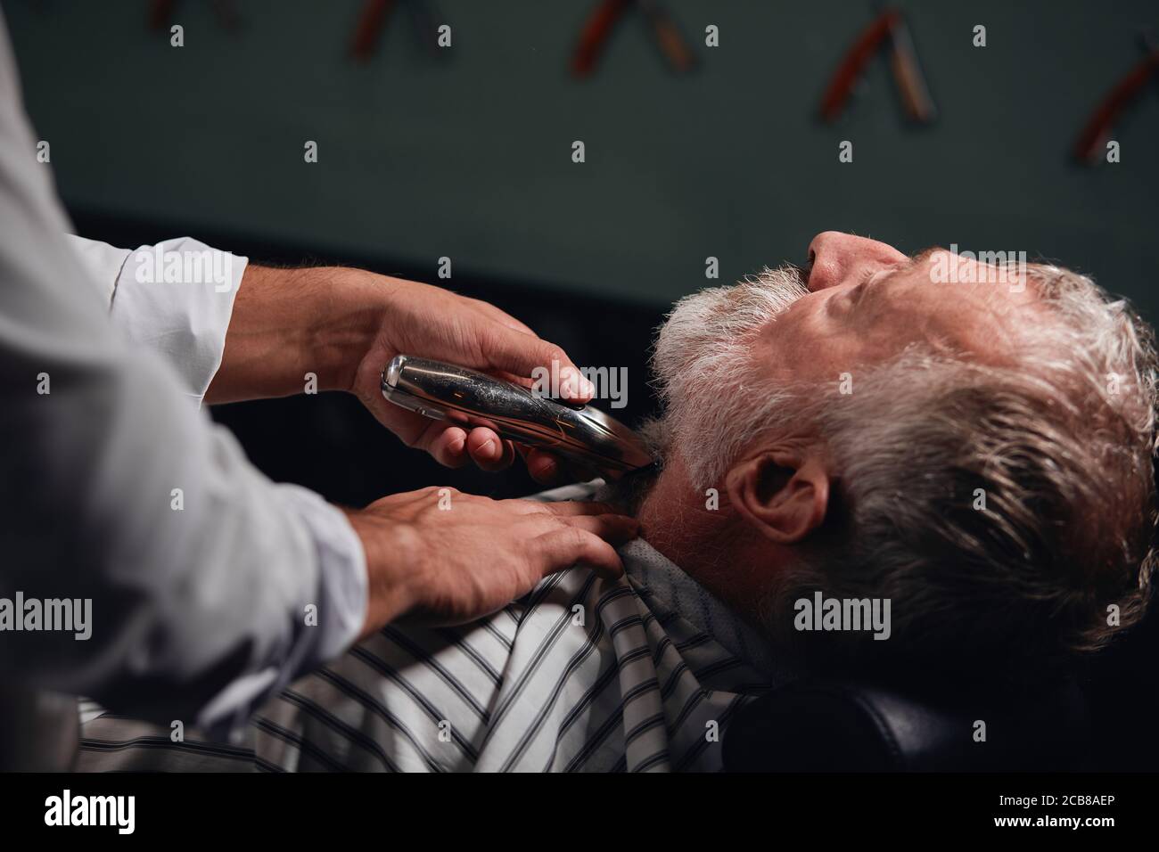 man shaving old man's grey beard at barber shop. close up back view ...