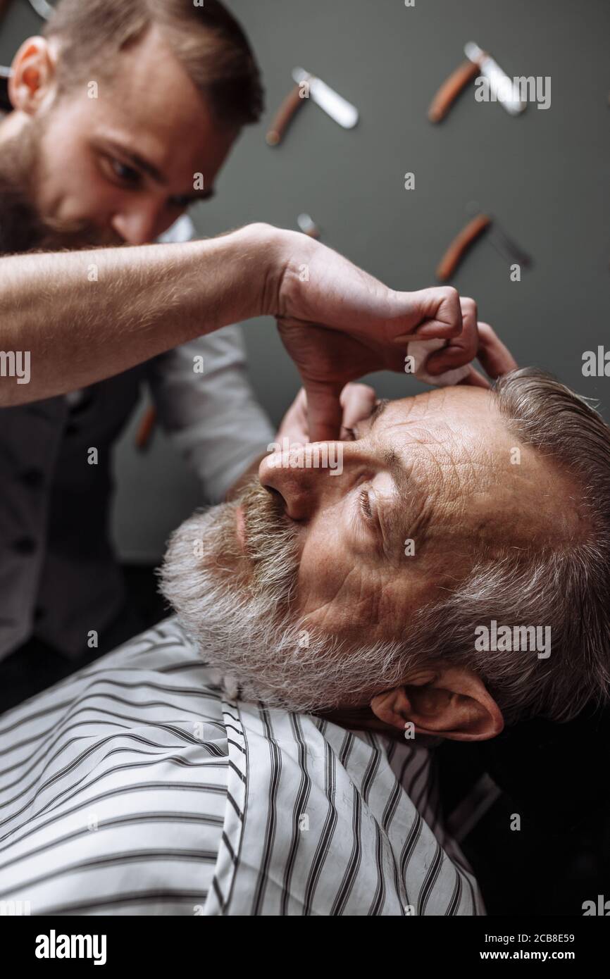 Caucasin old man getting his beard shaved by barber visiting hairtician ...