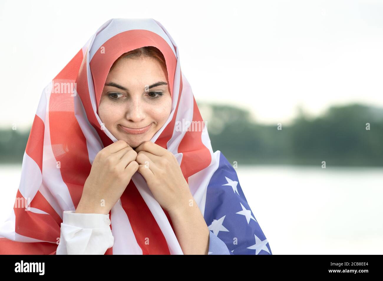 Portrait of young sad refugee woman with USA national flag on her head ...