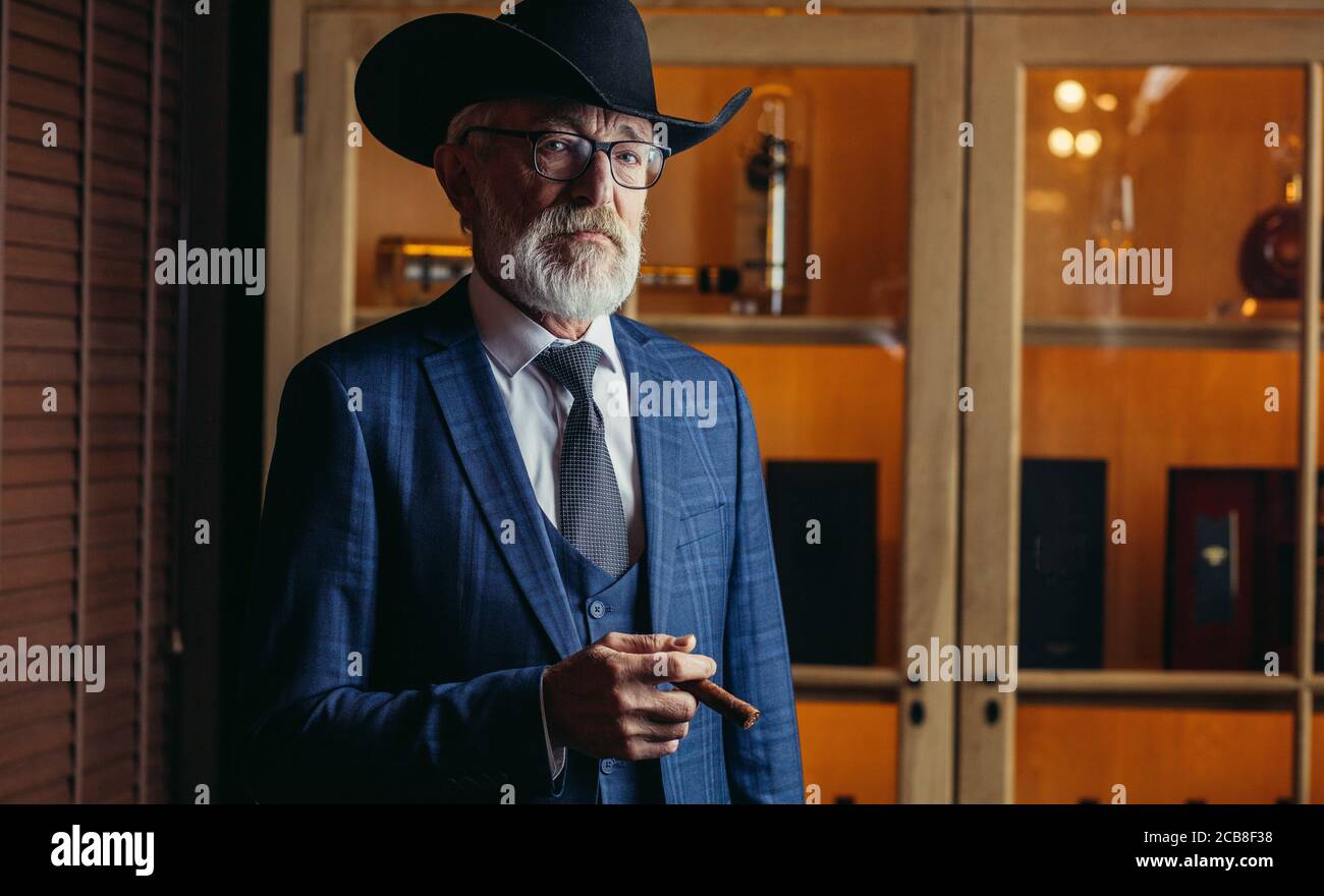 Thoughtful, selective, male aged investor in glasses, smoking cigar ...