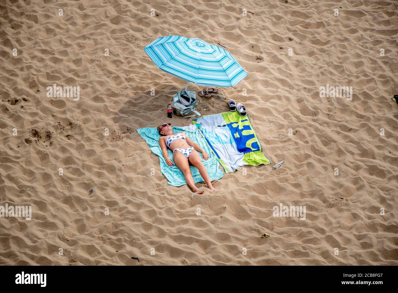 A woman sunbathing at the beachduring the heatwave. The beach is busy ...