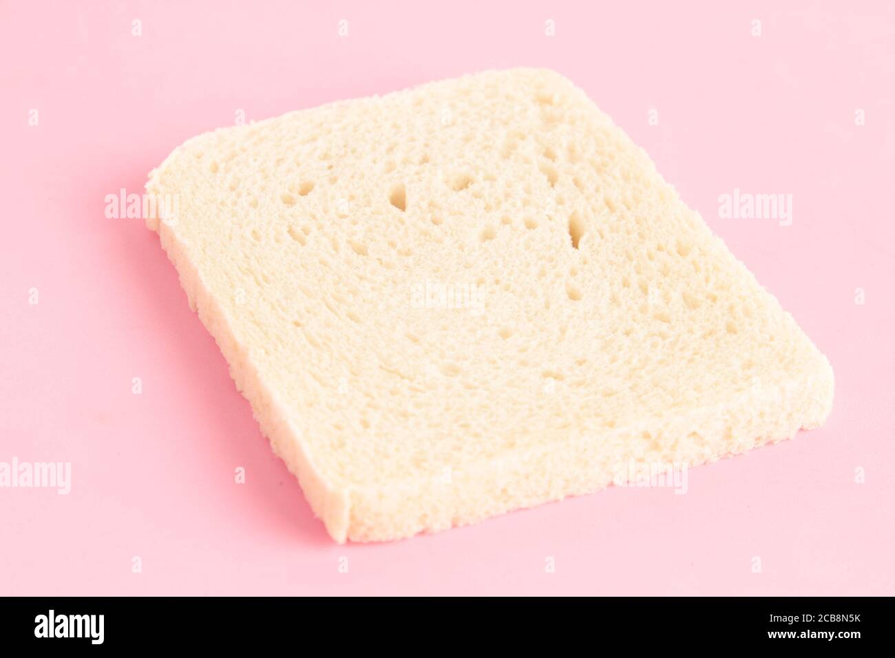 Closeup of a slice of white bread without the rind on a pink surface ...