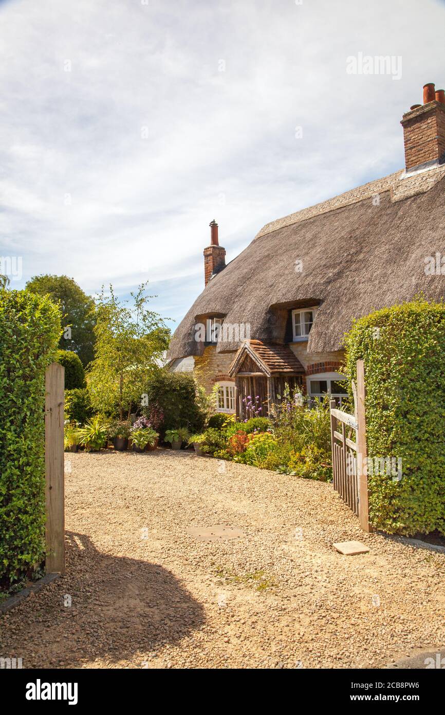 English country cottage with thatched roof seen through wooded entrance ...