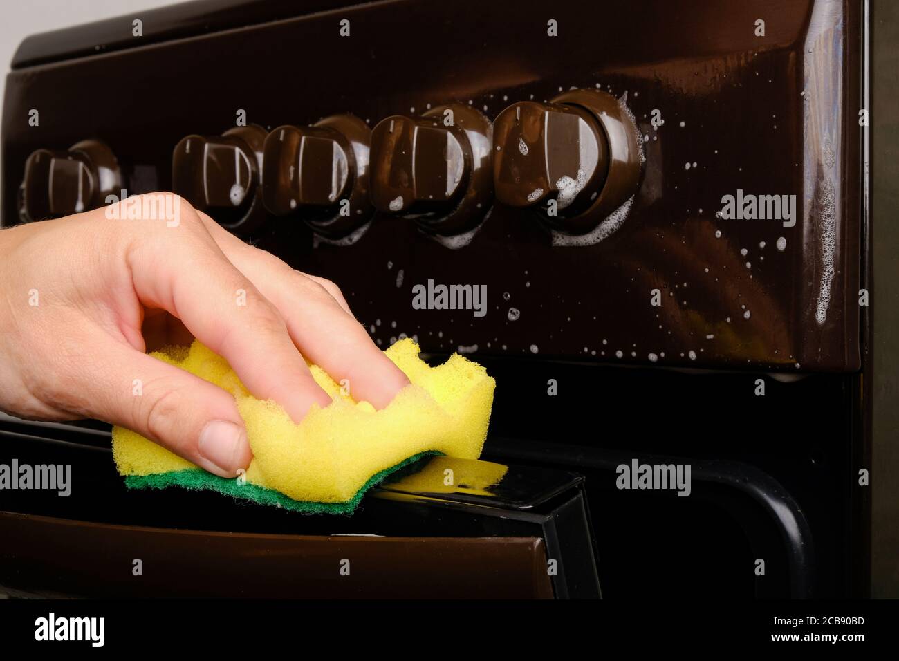 Female hand cleans the gas stove with a sponge with white foam ...