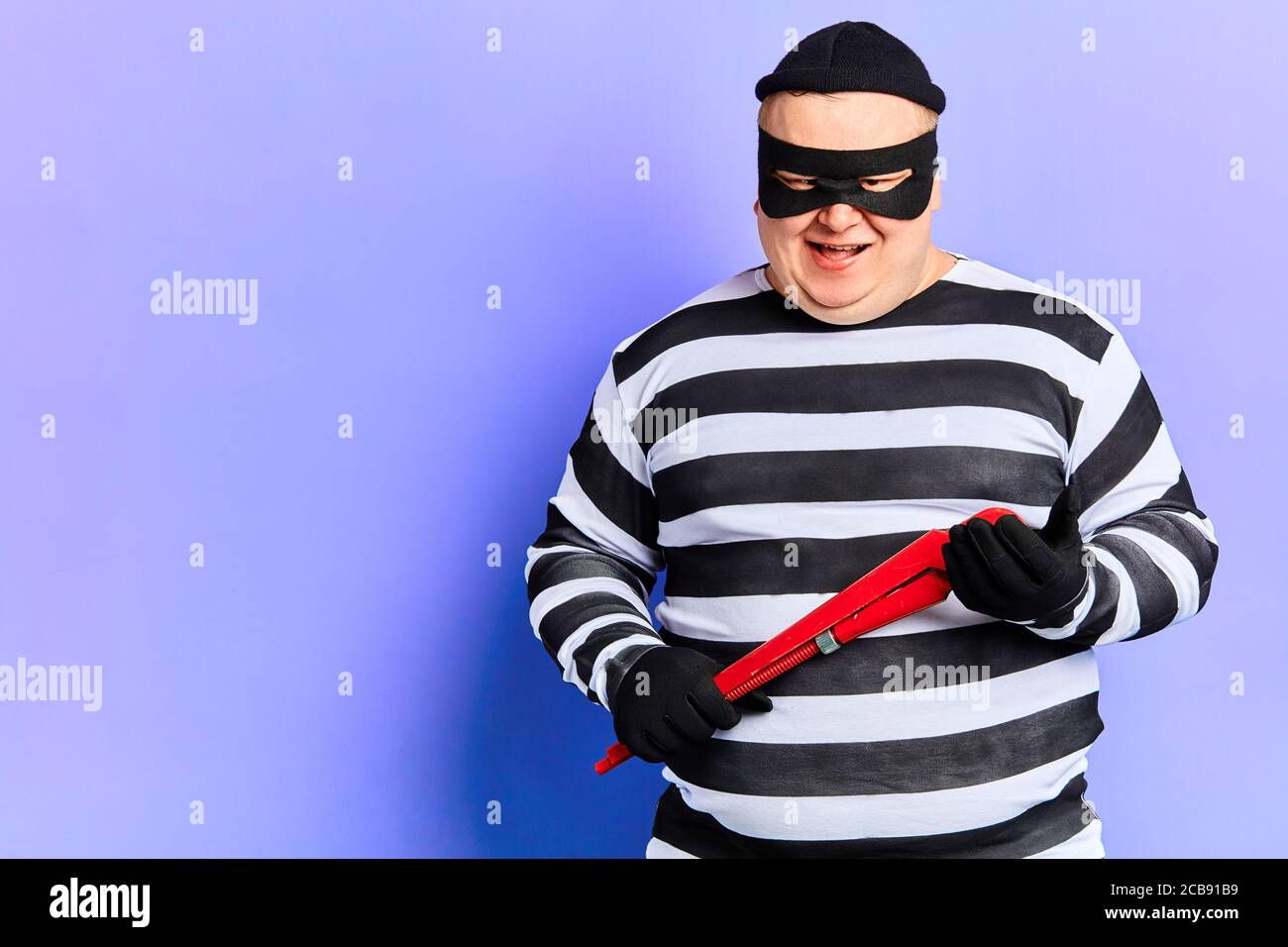fat prisoner in mask with pipe wrench in his hand looking at the camera ...