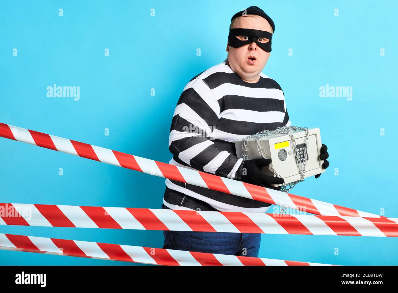 plump fat man with striped clothes in mask and hat carring safe. close ...