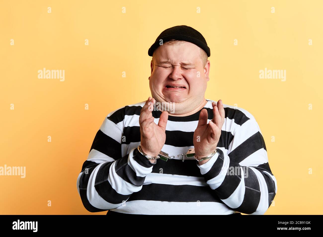 unhappy emotional thief with handcuff is crying. isolated yellow ...