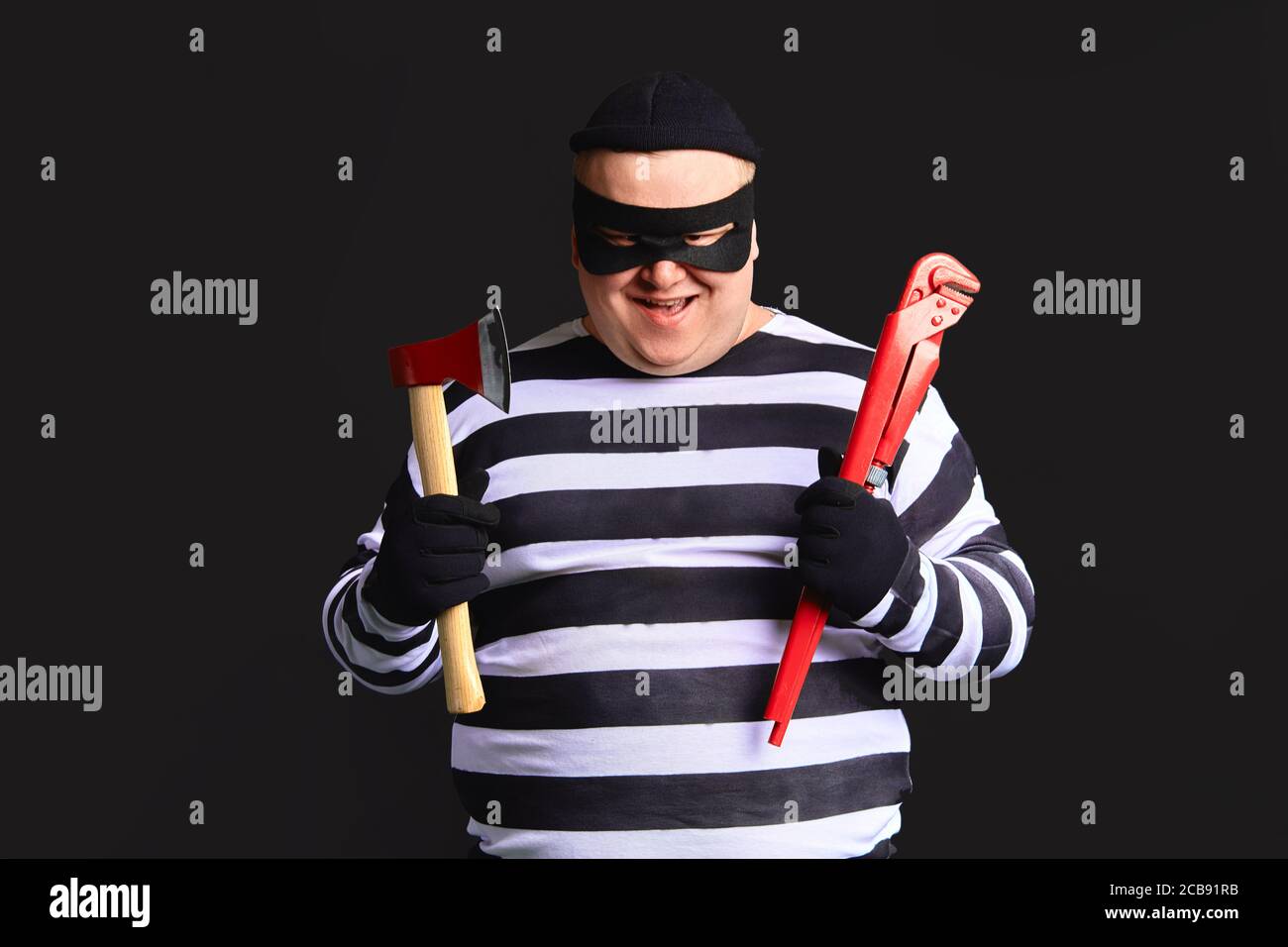 cheerful happy thief with a pipe wrench and ax in his hands looking at ...